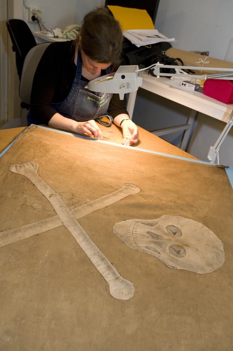 Konservator från Armémuseum tittar till en inlånad piratflagga från ...