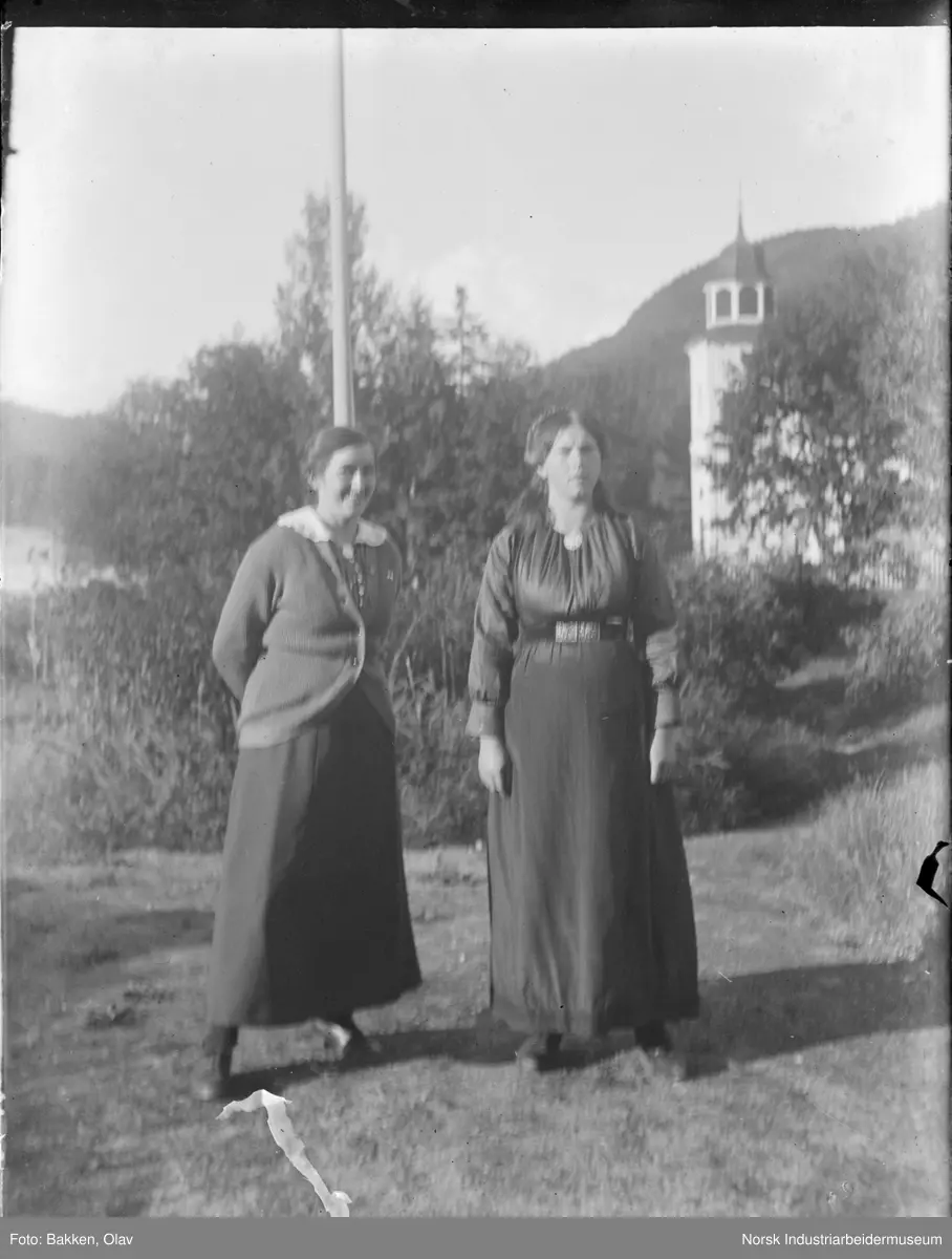 To damer oppstilt foran flaggstang i Prestegårdshagen. Gransherad kirke ...