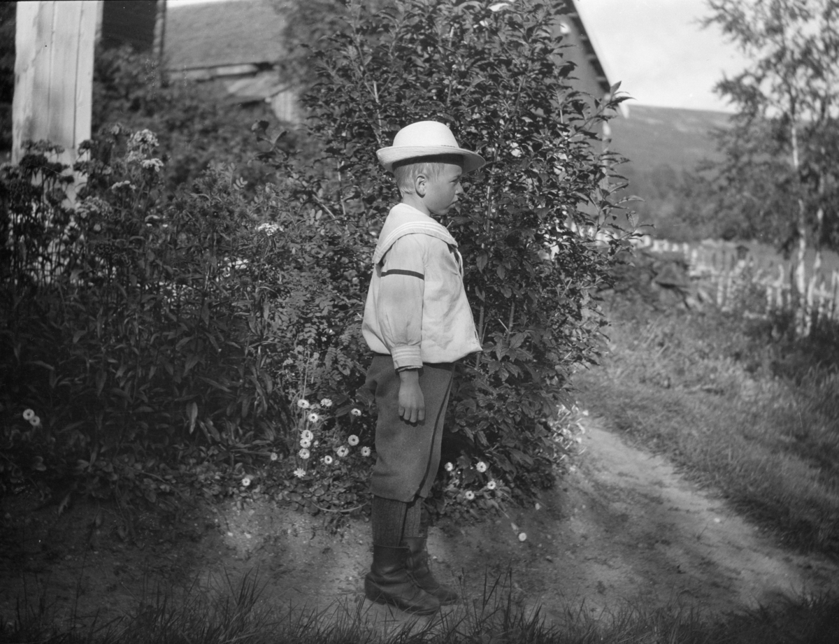 Liten gutt i matrosdress og hatt utenfor en bygning - Maihaugen ...