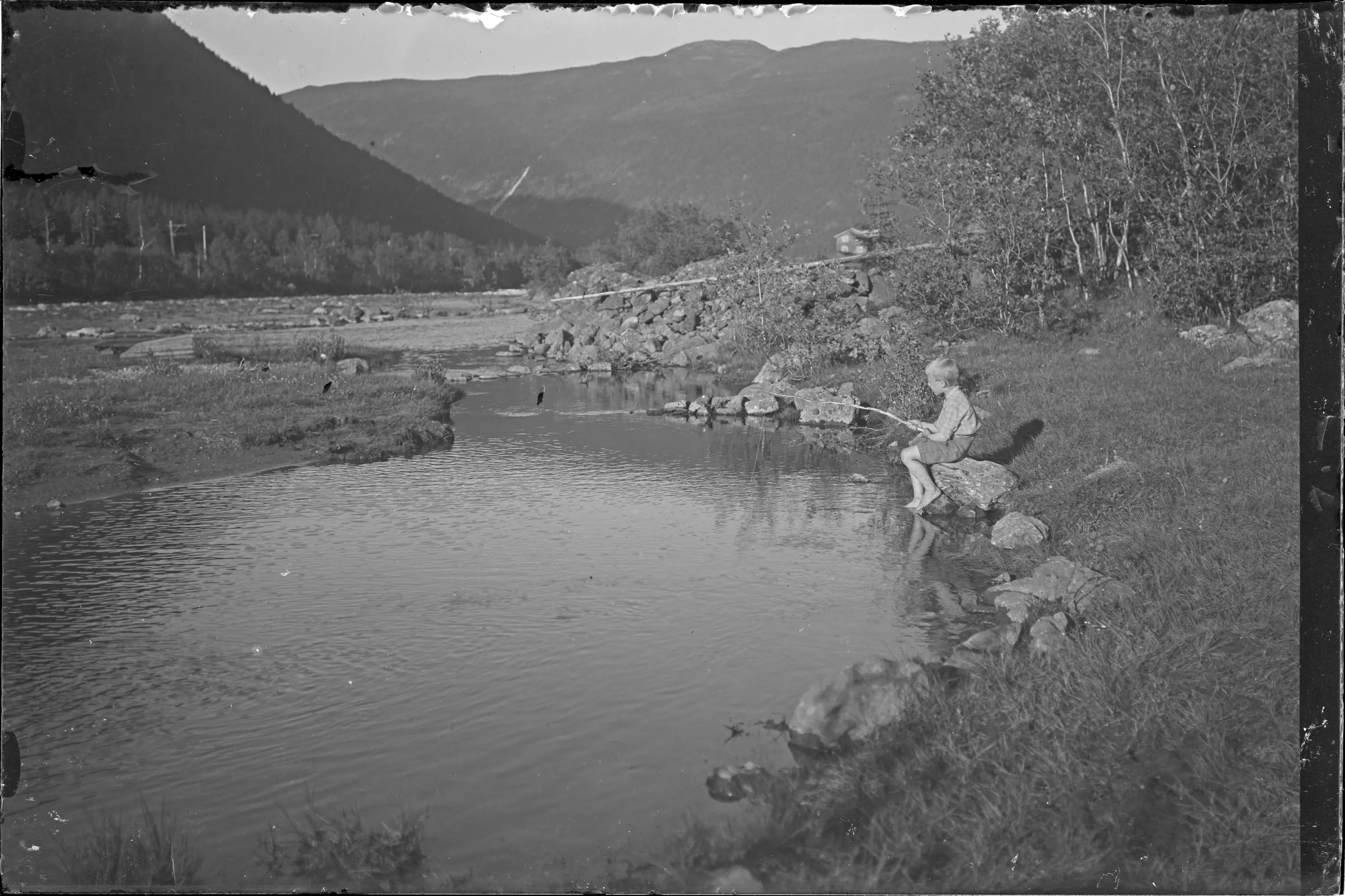 Gutt med hjemmelaget fiskestang sittende ved elvebredd i Månaelven ...