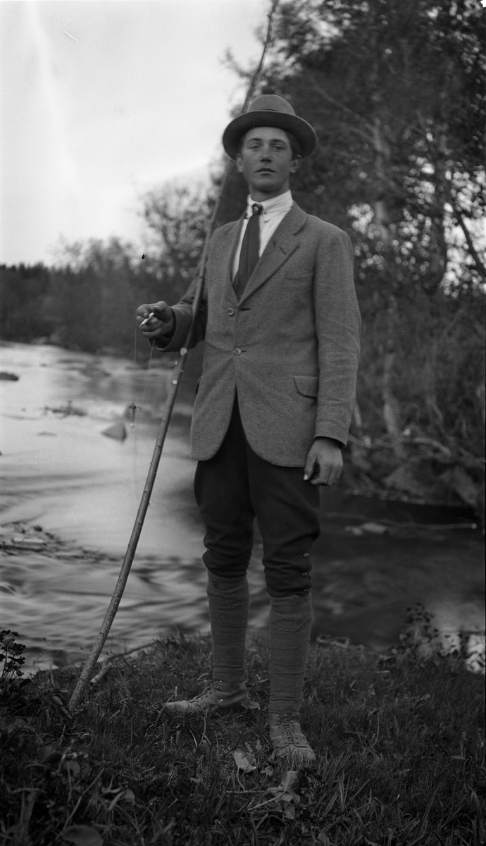 En uidentifisert mann med fiskestang ved en elvebredd, trolig Lenaelva ...