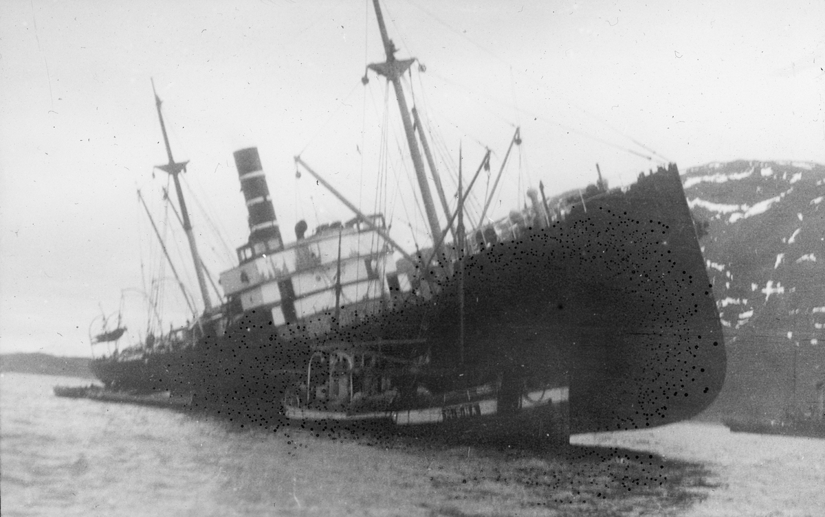 Dampskip med baugen i været. Tre mindre farkoster ligger langs skipets ...